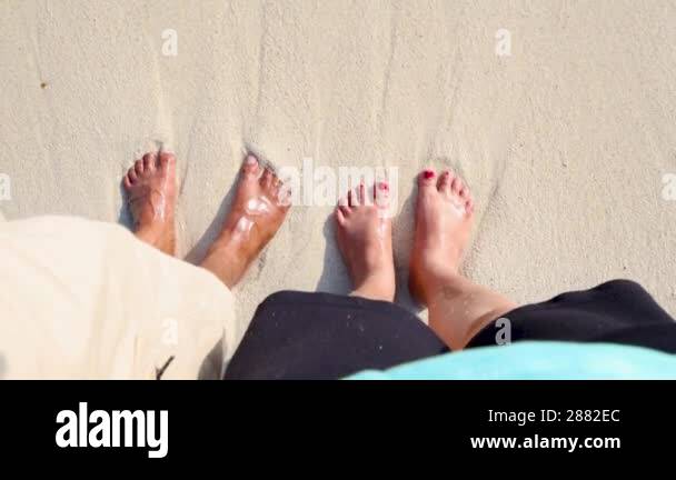 married couple feet washed by rolling sea waves on white sand beach at ...