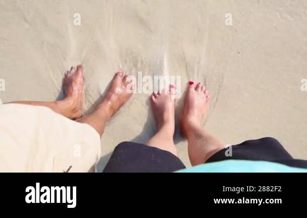 married couple feet with receding sea waves on white sand beach at ...