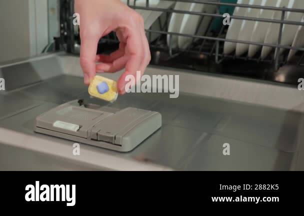 Close-up of hand placing dishwasher detergent tablet into dispenser of ...