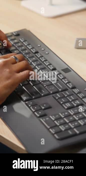 Vertical video Person at home office desk typing on PC keyboard next to coffee mug, close up ...