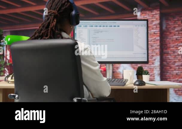 Programmer wearing headphones types code into PC, developing software ...