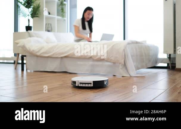 Young Asian woman in bedroom controlling robot vacuum cleaner. Concept ...