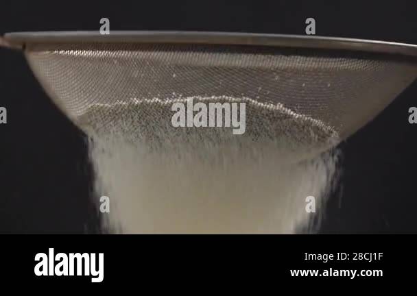 Whole wheat flour is sifted through a sieve on black background, slow ...