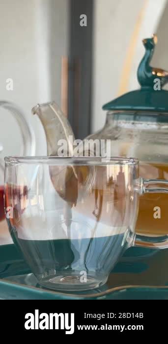Cinemagraph slow motion shot of pouring hot tea from glass teapot into ...