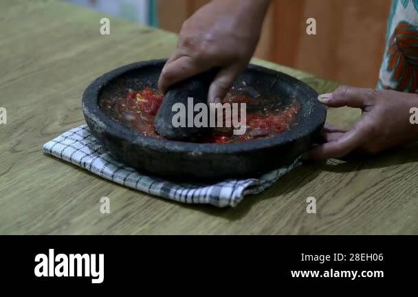 Indonesian woman's hands grinding spices on a stone mortar for sambal ...