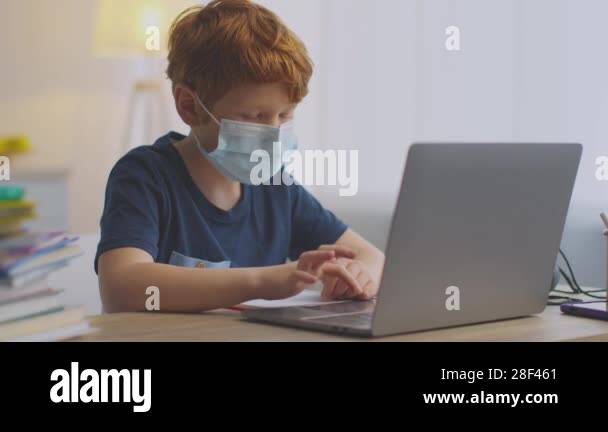A young boy studies diligently at home, focused on his laptop. He wears ...
