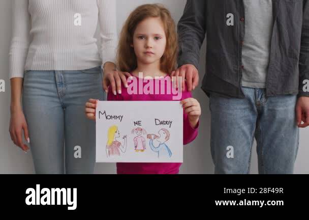 In a domestic setting, a young girl stands between her parents, holding ...