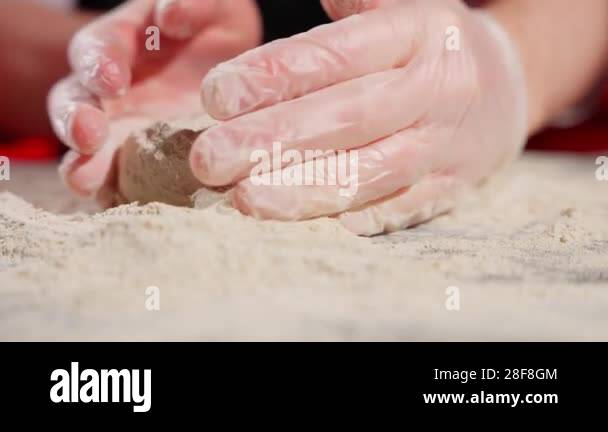 Close-up of gloved hands gently handling a ball of raw pizza dough ...
