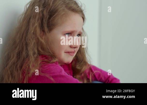 A young girl with curly hair shows signs of distress as she sits ...