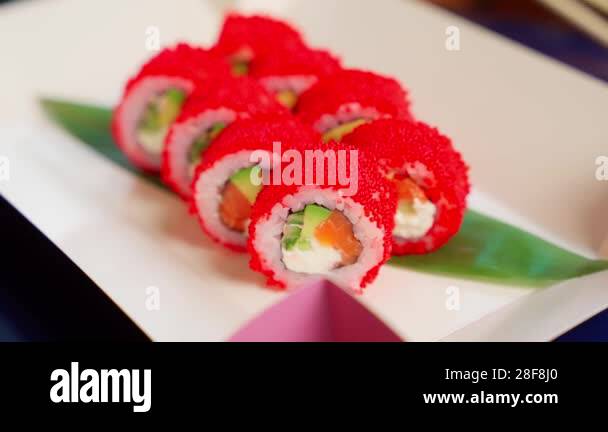 A plate of vibrant red tobiko-covered sushi rolls filled with salmon ...