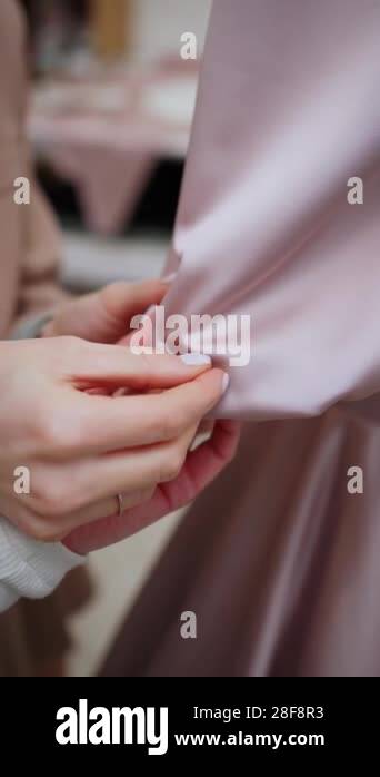 A close-up of hands gently holding and examining soft pink satin fabric ...