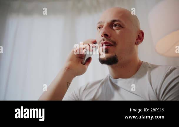 A bald man in a light-colored t-shirt is having a phone conversation ...