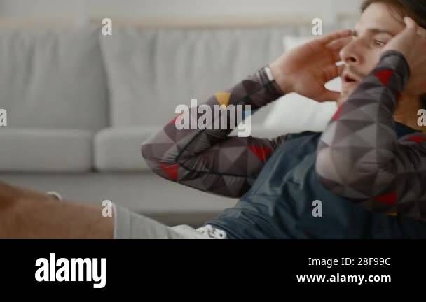 A young Caucasian man is exercising at home, performing core workouts ...