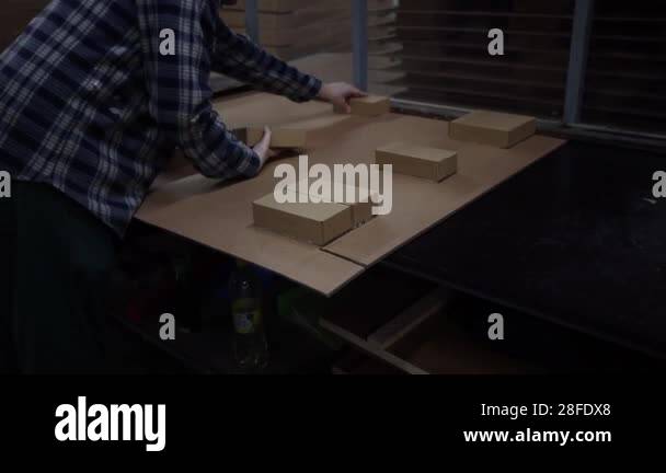 Hands arrange small cardboard boxes on a flat surface in a dimly lit ...
