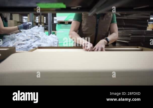 Individuals assemble cardboard boxes and handle plastic wrapped items ...