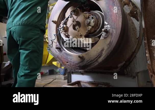 A factory worker inspects a large circular machine component. The ...