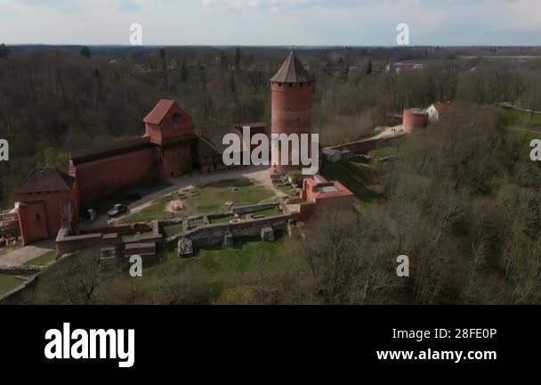 Red brick castle with a cylindrical tower, clock, and visible ruins ...