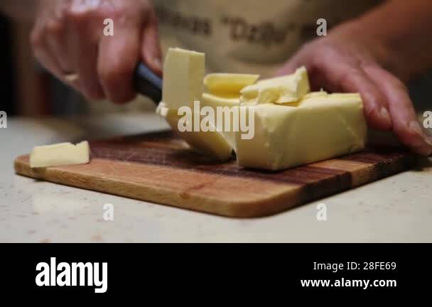 A person slices a block of butter into smaller pieces on a wooden ...