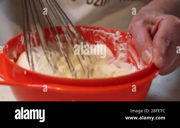 A metal whisk stirs a creamy mixture in an orange bowl on a light ...