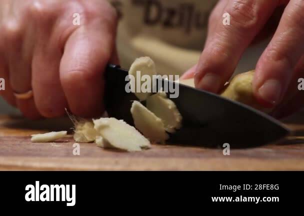 Hands slice fresh ginger root into thin, even pieces on a wooden ...