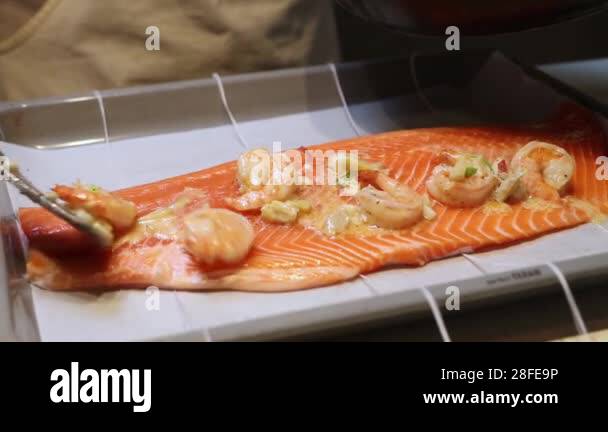 A raw salmon fillet topped with seasoned shrimp, herbs, and butter on a ...