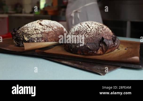 Two loaves of dark bread rest on parchment lined trays, dusted with ...