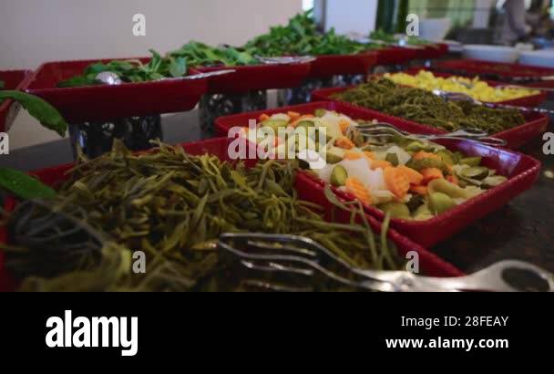 An array of colorful vegetables and pickles in red trays with serving ...