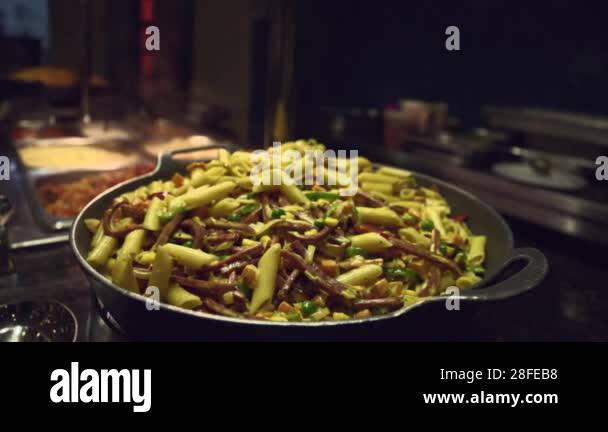 A large skillet of penne pasta with sliced vegetables and herbs is ...