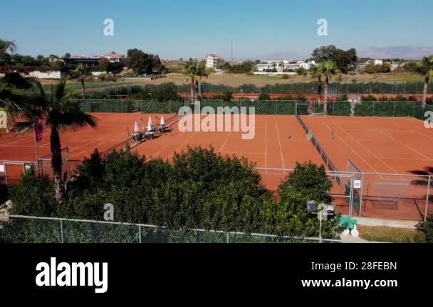 Multiple clay tennis courts are surrounded by palm trees and lush ...