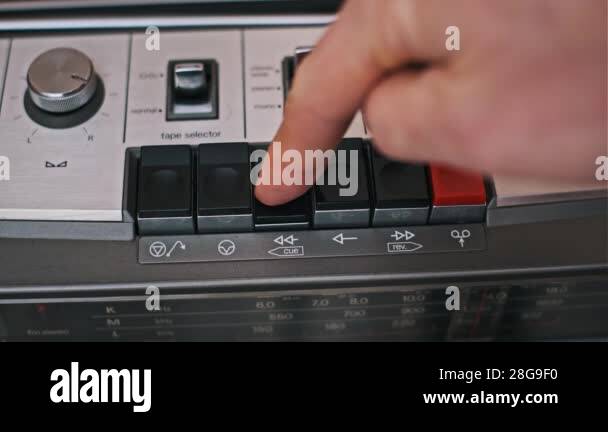 A hand is shown pressing the rewind button on a retro vintage tape ...