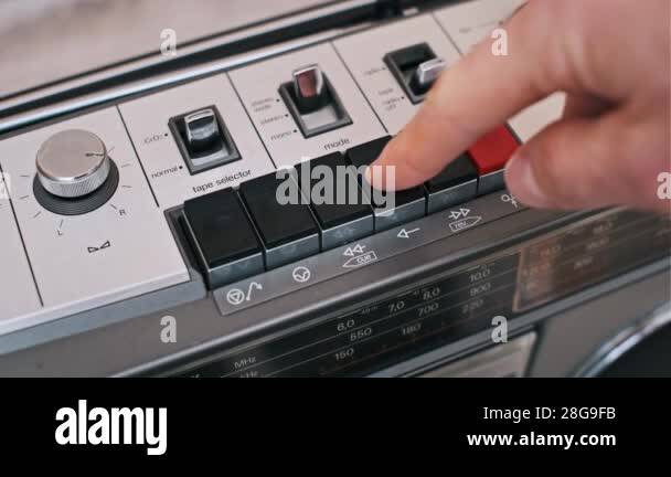 A finger presses the play button on a silver and black retro boombox ...