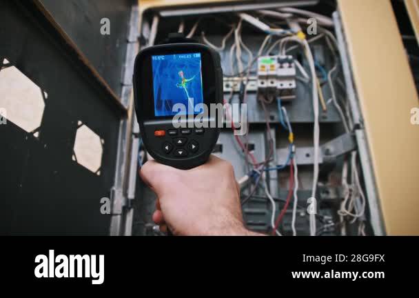 Hand holding a thermal camera inspects inside an electrical box, with ...