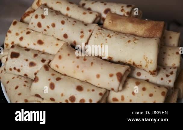 A hand reaches in to take a rolled pancake from a stack of many on a ...