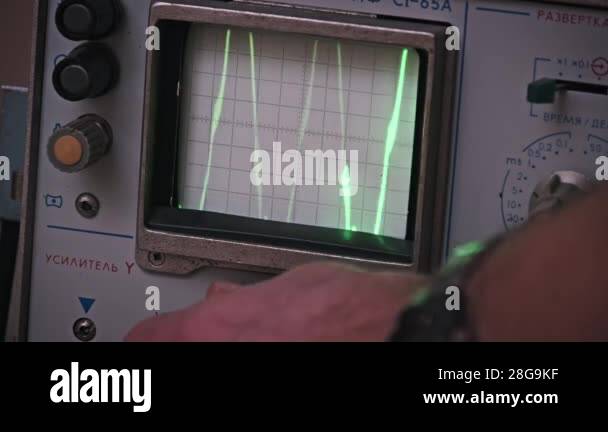 A person adjusts a vintage oscilloscope as the green wave patterns ...