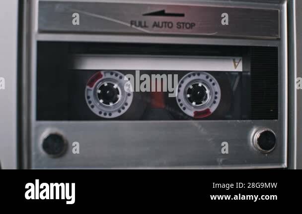 A close-up of a transparent cassette tape with red accents turning ...