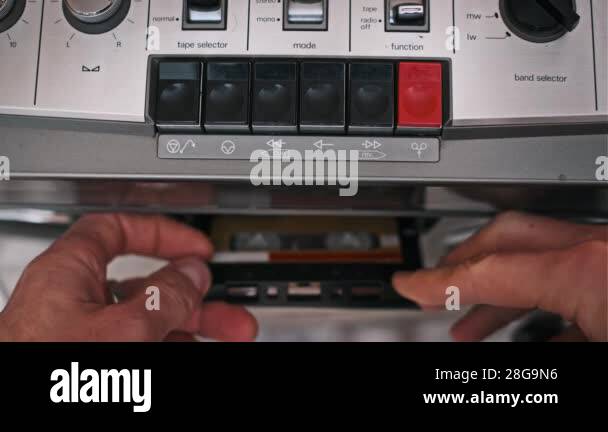 Close-up of hands inserting a cassette into a vintage tape player and ...
