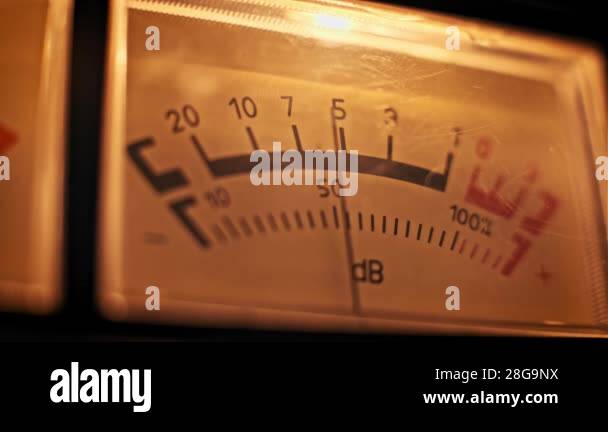 A close-up of a vintage analog VU meter with a warm amber glow ...
