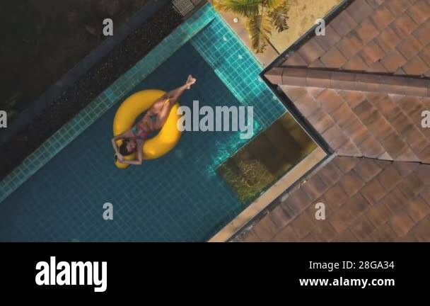 Woman floats on yellow inflatable ring in a turquoise resort pool in ...