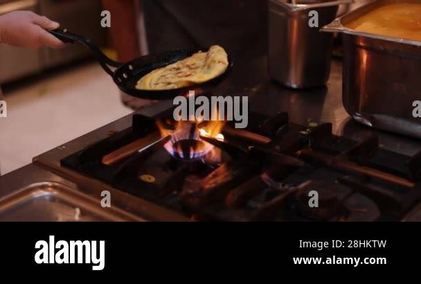 Professional chef flips golden omelette over sizzling gas stove flame. Culinarian prepares ...
