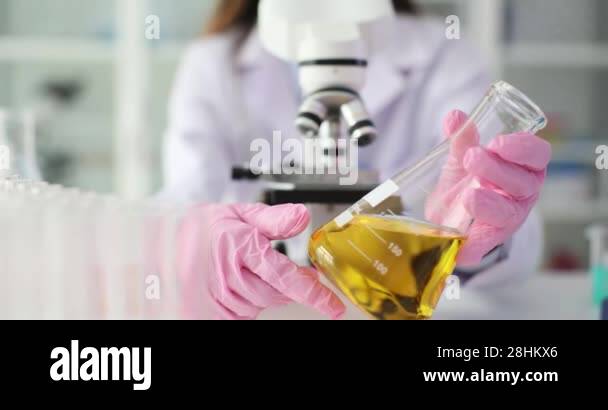 Woman scientist inspects reaction of liquid to slight tilts. Chemist observes yellow fluid in ...