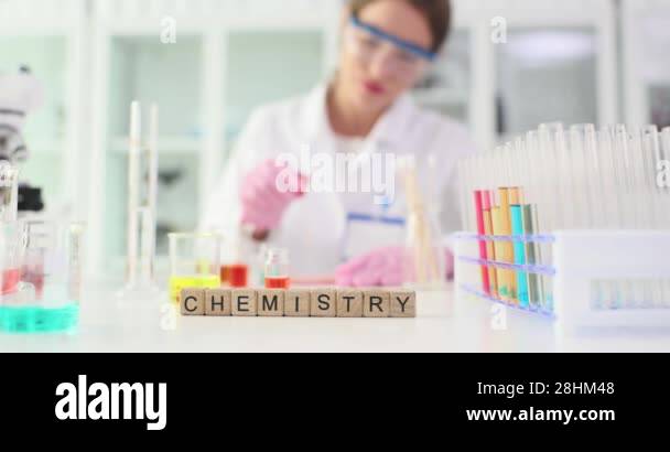 Table adorned with wooden cubes forming word CHEMISTRY. Focused woman ...