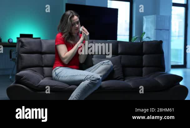 Feverish woman checks body temperature with thermometer and blows nose ...