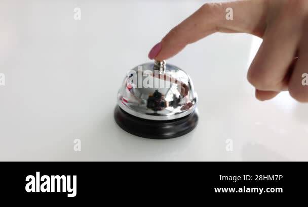 A hand firmly pressing down on a shiny metal service bell placed on a ...