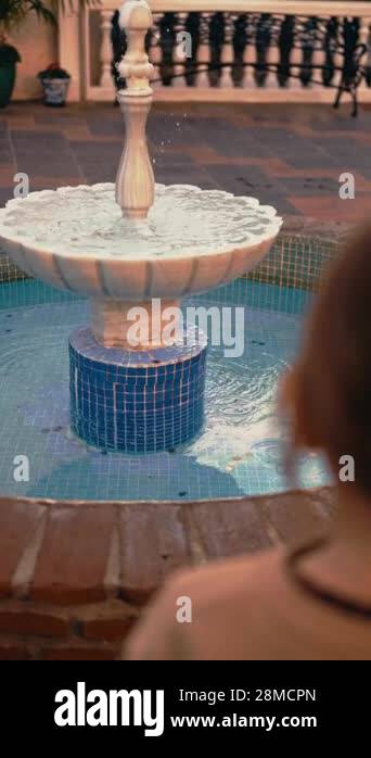 Over-the-shoulder view of a young girl tossing a coin into a fountain ...