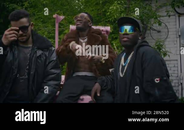 Medium handheld shot of cool Black male rapper in fur coat vaping and ...