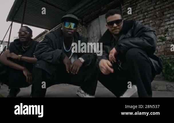 Full shot of group of diverse three cool guys in black baggy clothes and chains on neck ...