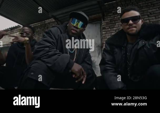 Handheld low angle shot of cool Black male rapper in sunglasses and cap ...