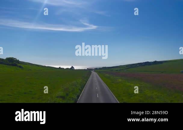 English countryside road stretches through vibrant green hills under a ...