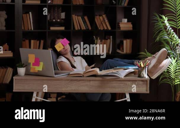 Tired female student at a desk in a beautiful library with her feet up on the table with ...