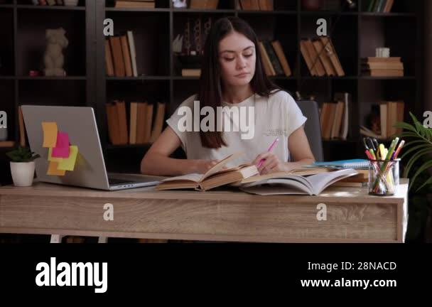 Tired young woman yawns with hand over mouth studying for exams in a ...